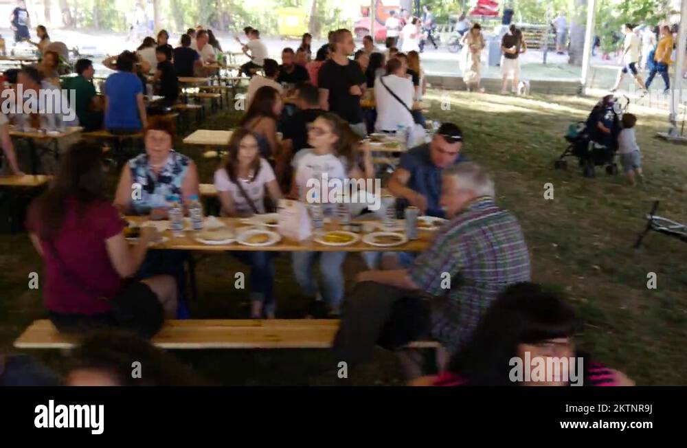 People crowd eating during food festival sit at tables under a big ...