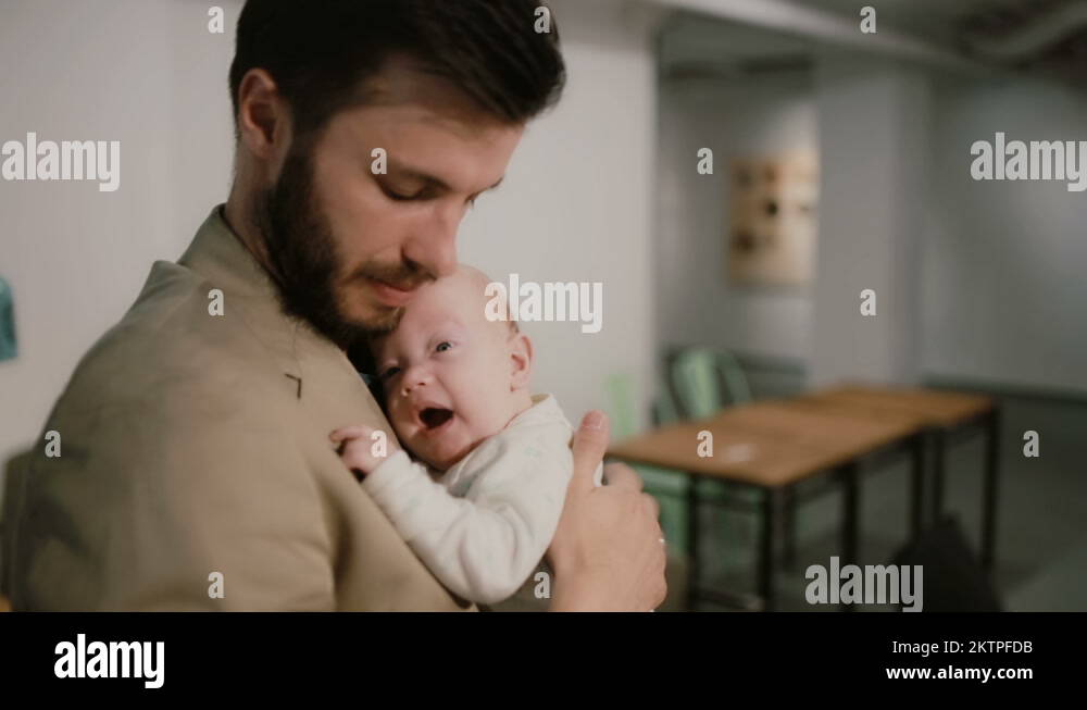A young man is holding a baby on his arms and talking, kissing him on a ...