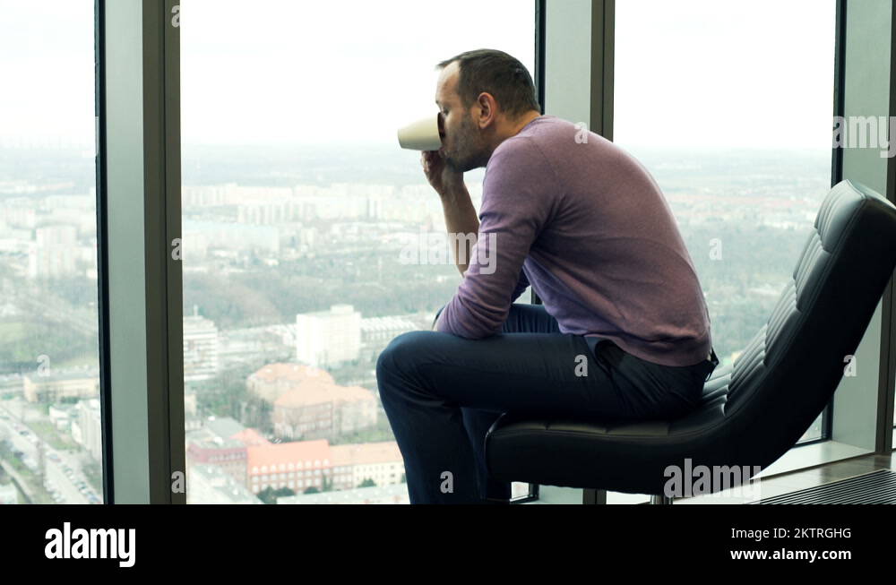 Sad, unhappy man drinking coffee sitting on chair by window at home ...