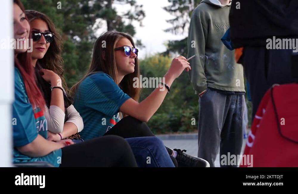Cute pretty teenager girl sit smoking cigarette in public place slow ...