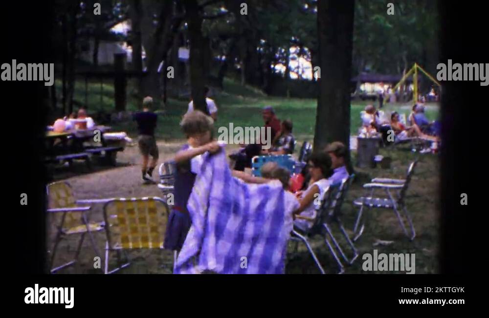 1963: adults and children gather for a picnic in a park by a playground ...