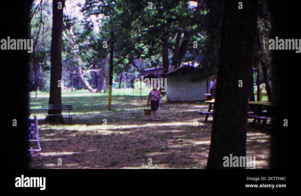 1963: people carry baskets and chairs into picnic area shaded by tall ...