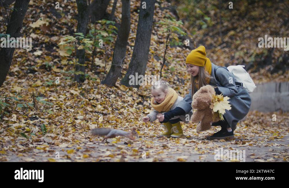 A cute little girl with blonde hair and her mom feed the red squirrels ...