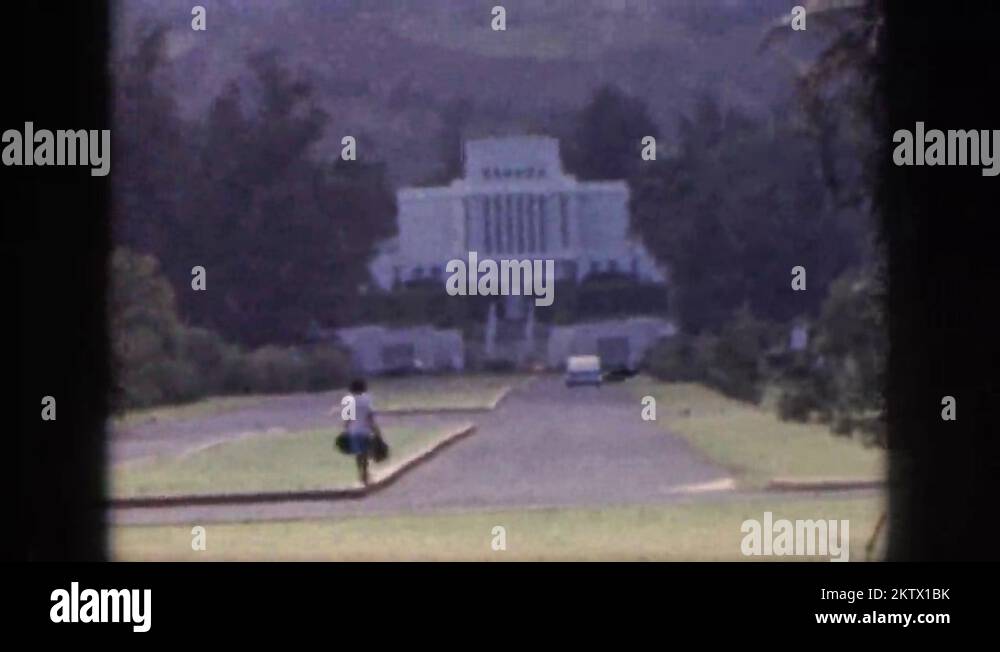 1961: woman with bags waiting on a curb in front of stately white ...