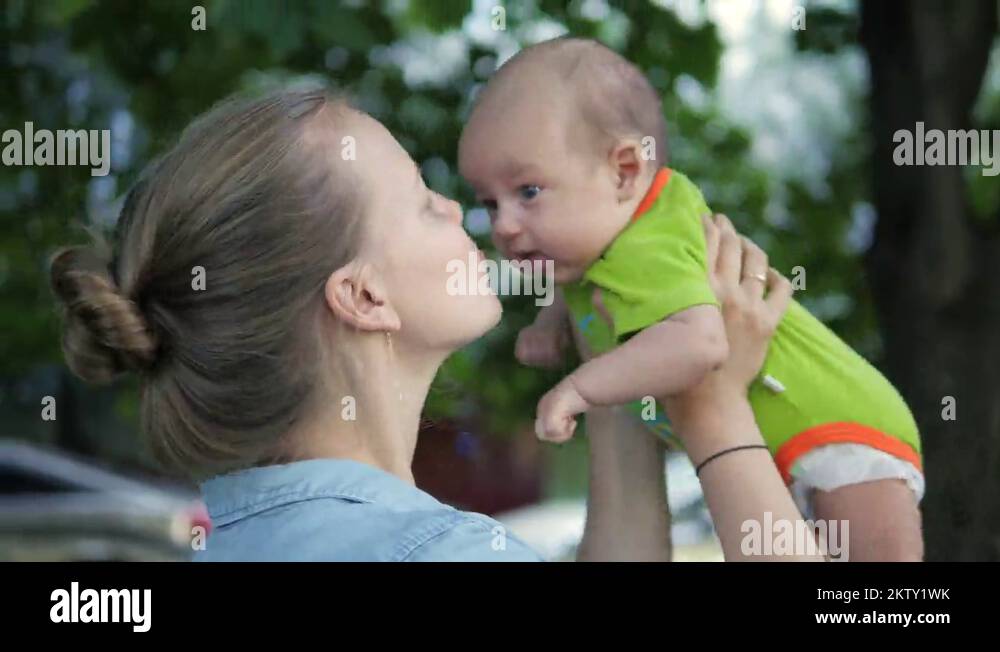 Young mother raising a baby in the air, kissing and making him laugh ...