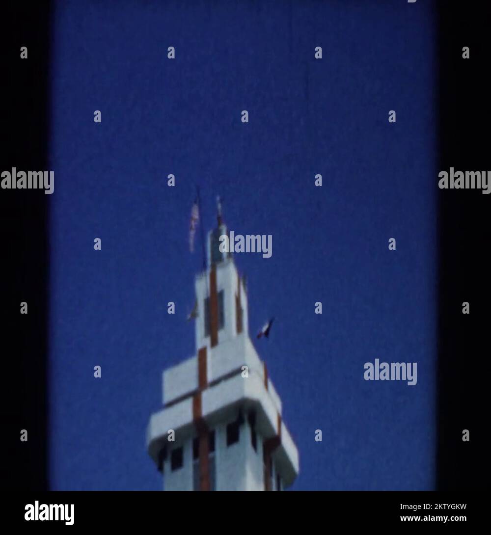 1958: a tall magnificent tower with flags stands high up in the sky ...