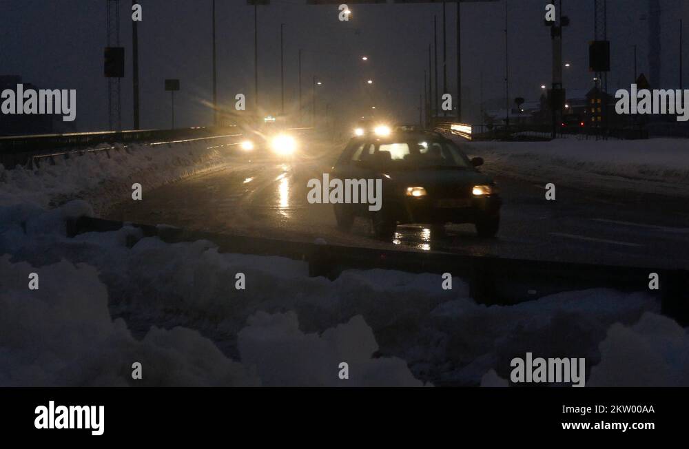 Cars with lights on driving in a highway at night during heavy snow ...