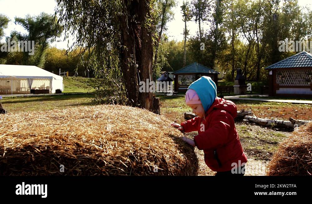 Two little girls having fun on haystack. They jump and climb onto it ...
