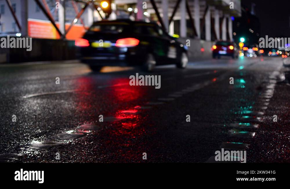 Traffic light and rainy street at night. Cars passing by on wet asphalt ...