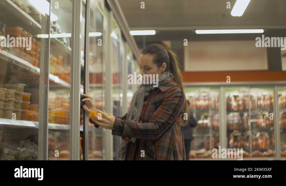 Young woman shopping at supermarket. Opening fridge to pick up ...