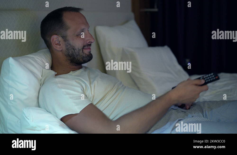 Young, happy man watching TV lying on bed at home at night Stock Video ...