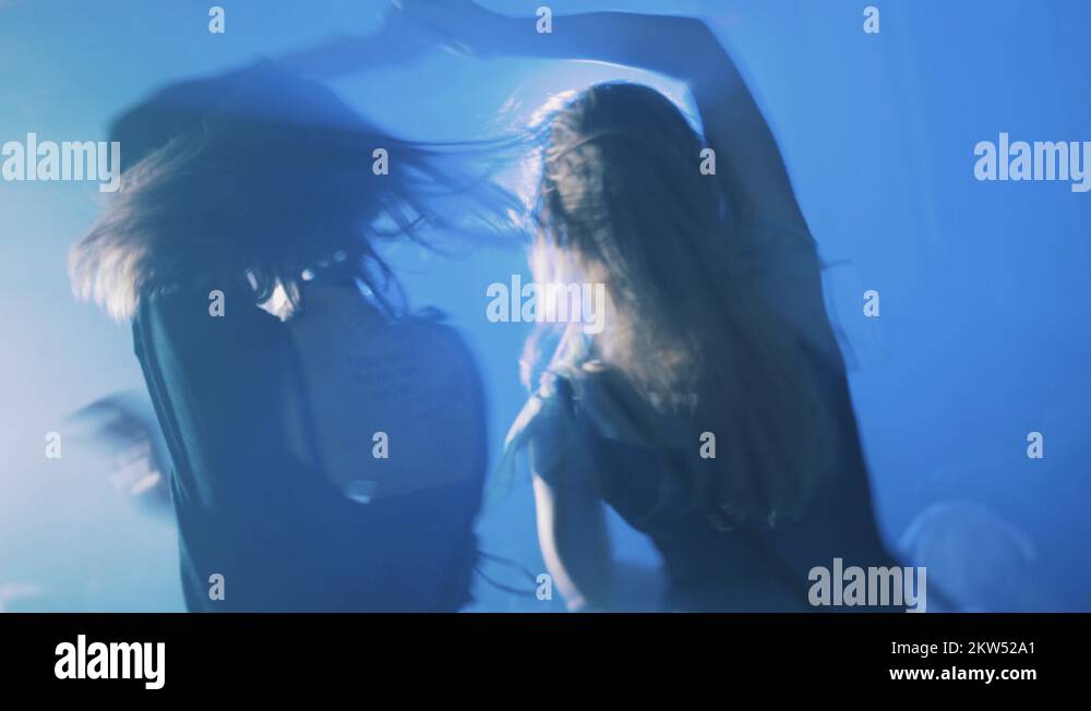 Two girls silhouettes dance on scene at night club in beams of bright ...