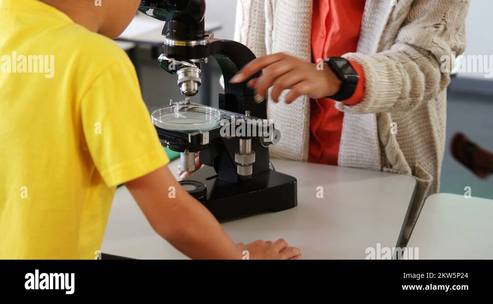 Teacher assisting schoolboy with microscope in classroom Stock Video ...