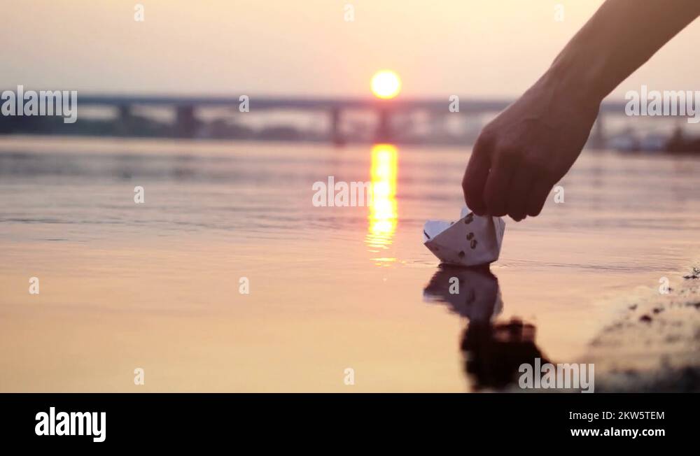 Man's hand putting paper boat on the water and pushing it away during ...