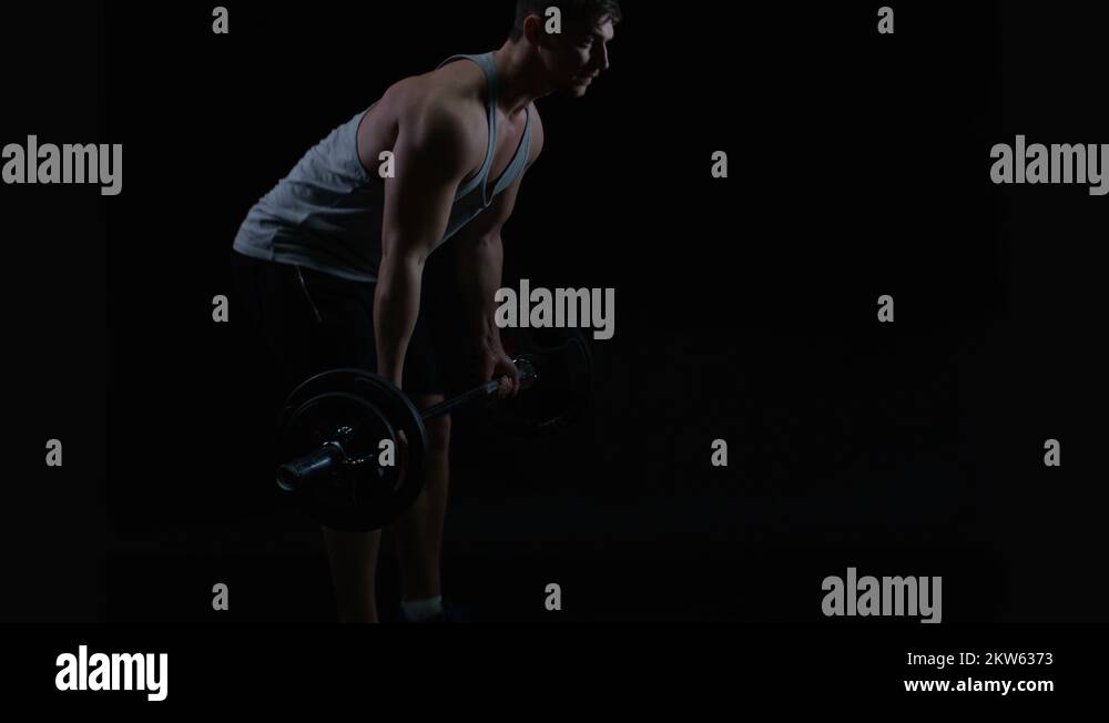 4K Fit young man with muscular physique lifting weights against black ...