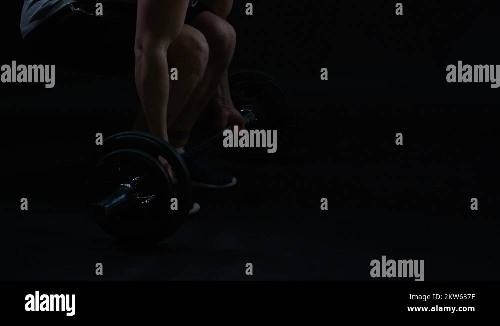 4K Fit young man with muscular physique lifting weights against black ...