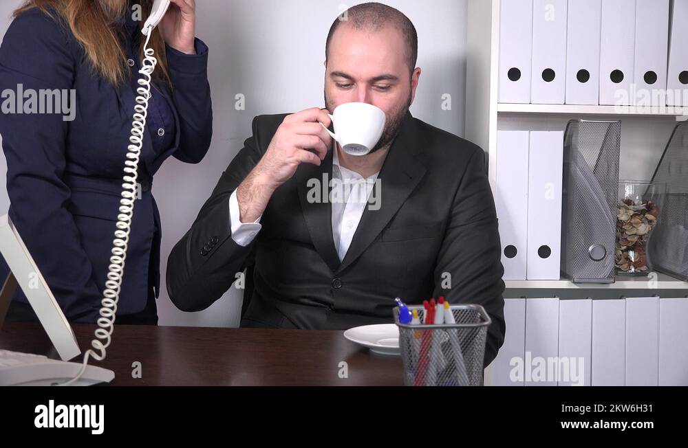 Two business people inside office male drinking coffee female telephone ...