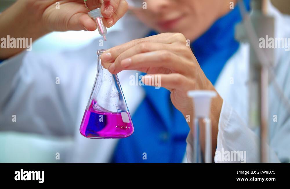 Medical lab worker dripping reagent in chemical liquid at lab flask ...