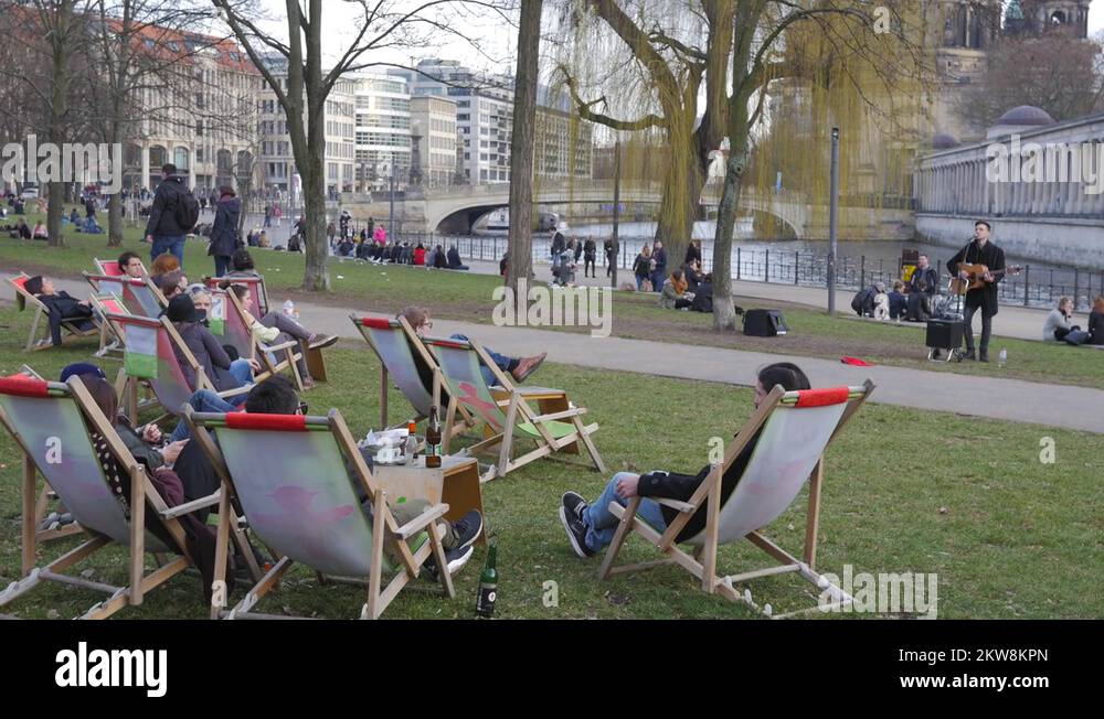 Berlin city center park, young people sit rest on chaise chairs of park ...