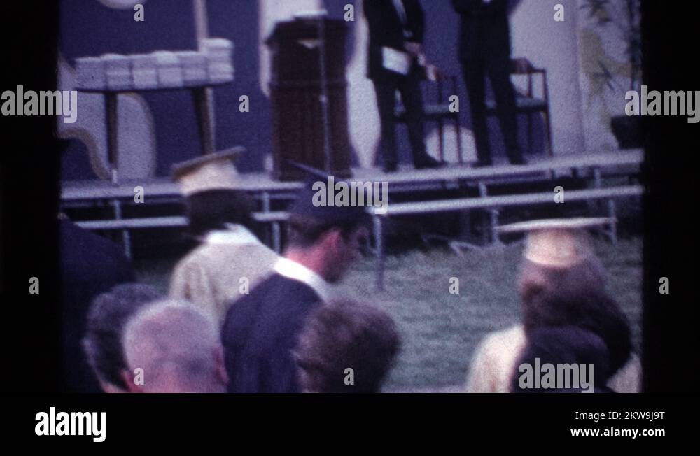 1969: two men in dark suits stand on platform during graduation ...