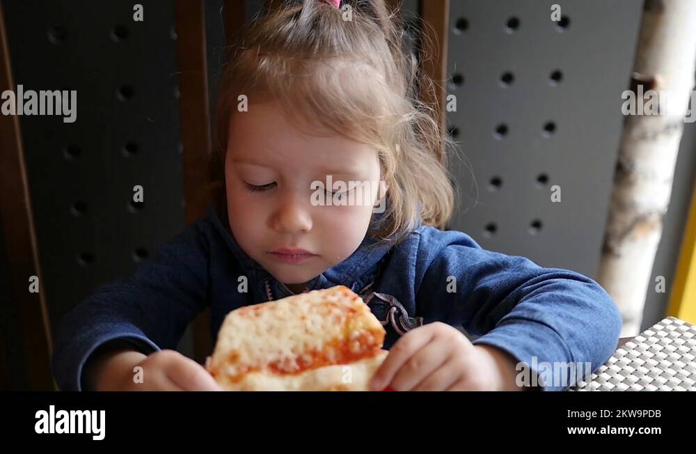 Little child girl eating a tasty piece of pizza in a pizzeria ...