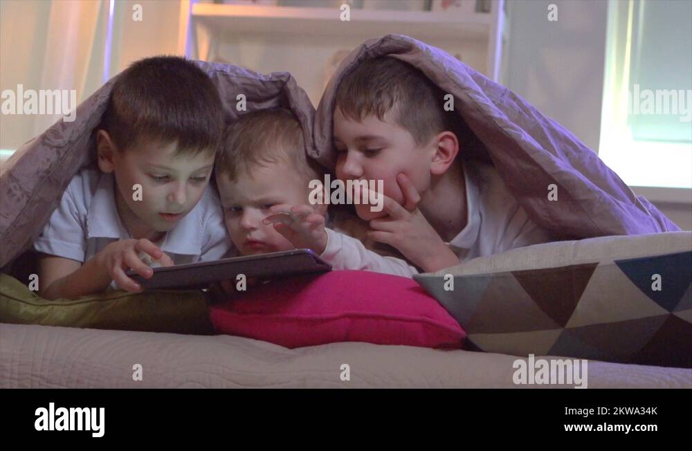 Three little boys with tablet computer in a dark room. Kids playing ...