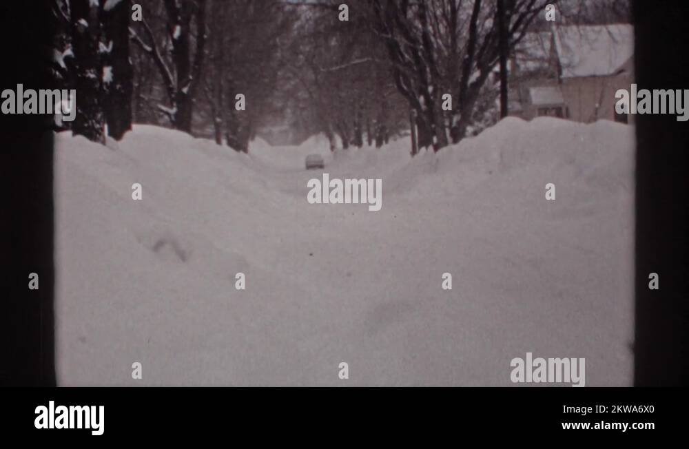 1971: snow filled road with trees on each side and a car parked far ...