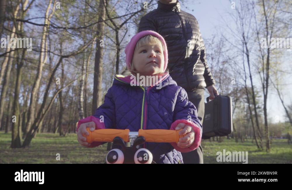 Dad rolls his little daughter on a scooter, low angle gimbal shot, slow ...