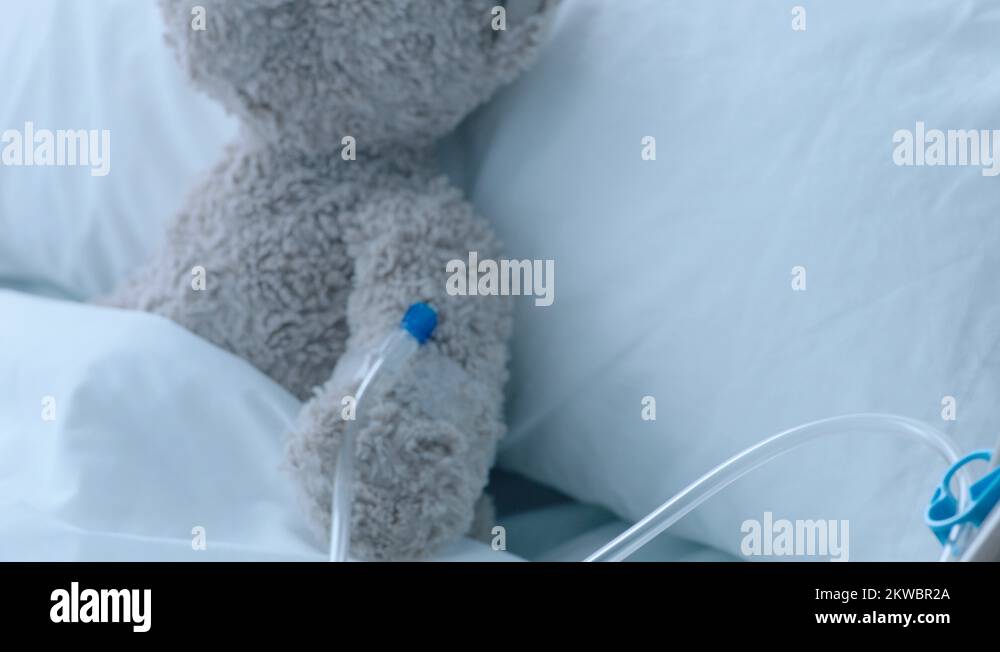 A teddybear stuffed animal with an IV recovering in a hospital bed next ...