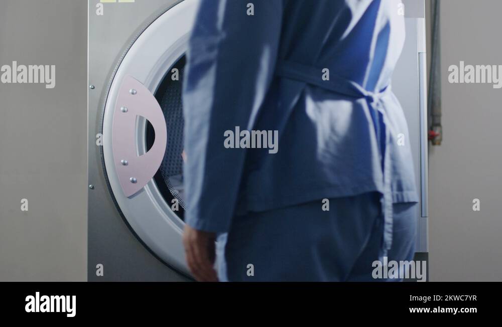 Woman loading uniform in industrial washing machine. Industrial washing ...