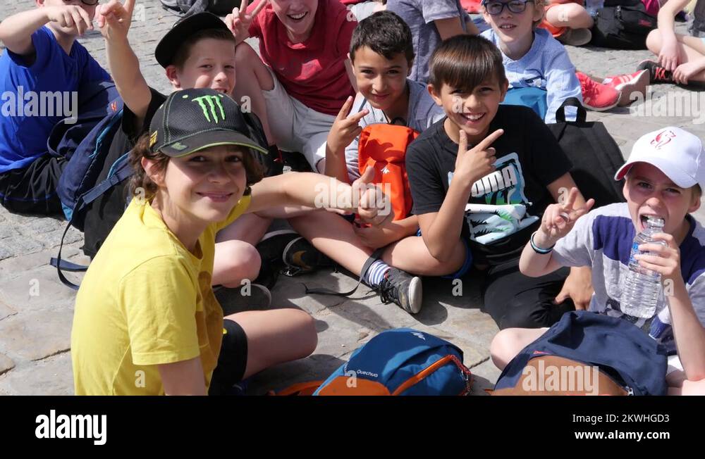 Children excursion touristic group sit on cobblestone square under ...
