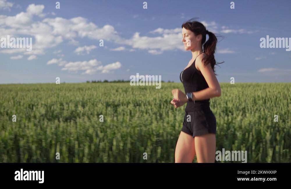 Young woman runner is runing across the field in a sporty uniform. Slow ...