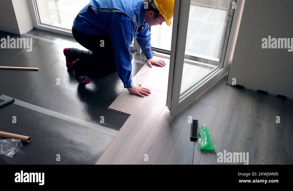 Skilled handyman guy with yellow hard hat installing laminate boards on ...