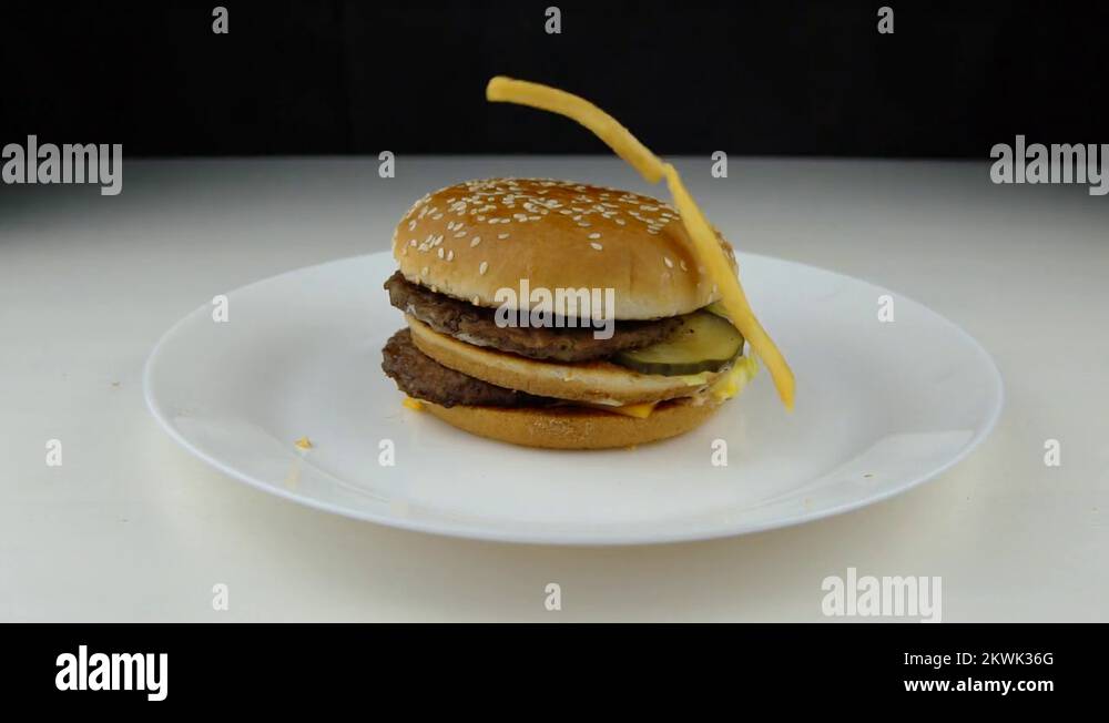 Fried potato chips falling down on hamburger, slow motion, fast food ...