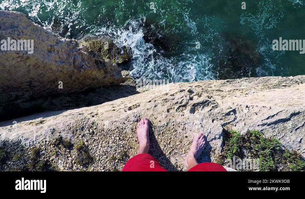 A man stands on the edge of a cliff by the sea - first person view ...