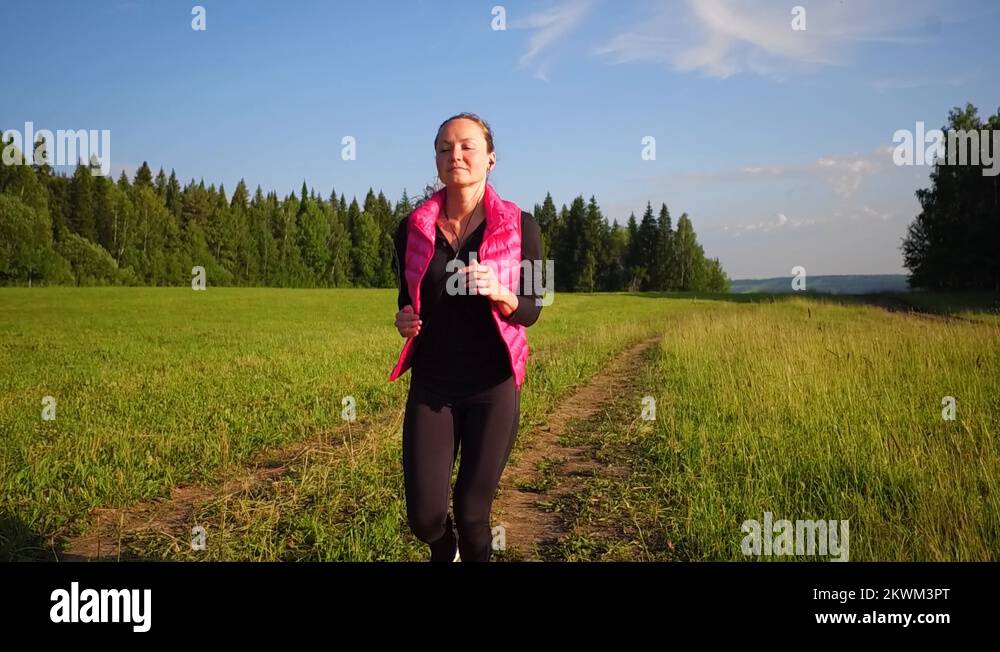 Pretty girl wearing sportswear and running in green forest at mountain ...