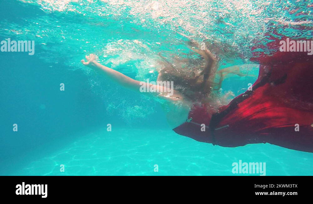 Young blonde girl in long red dress jumps into the swimming pool Stock ...