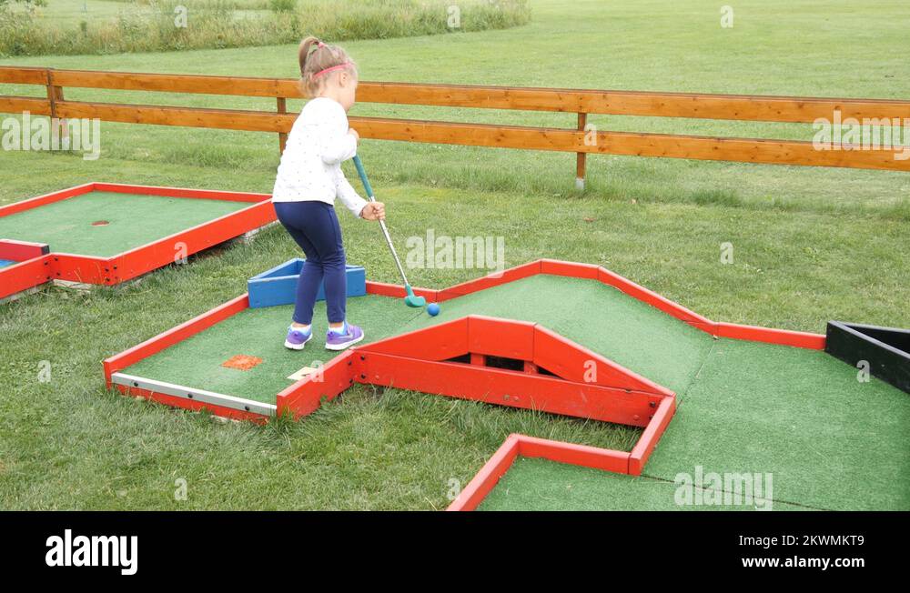 Playful childhood - little child girl enjoy play mini golf in outdoor ...