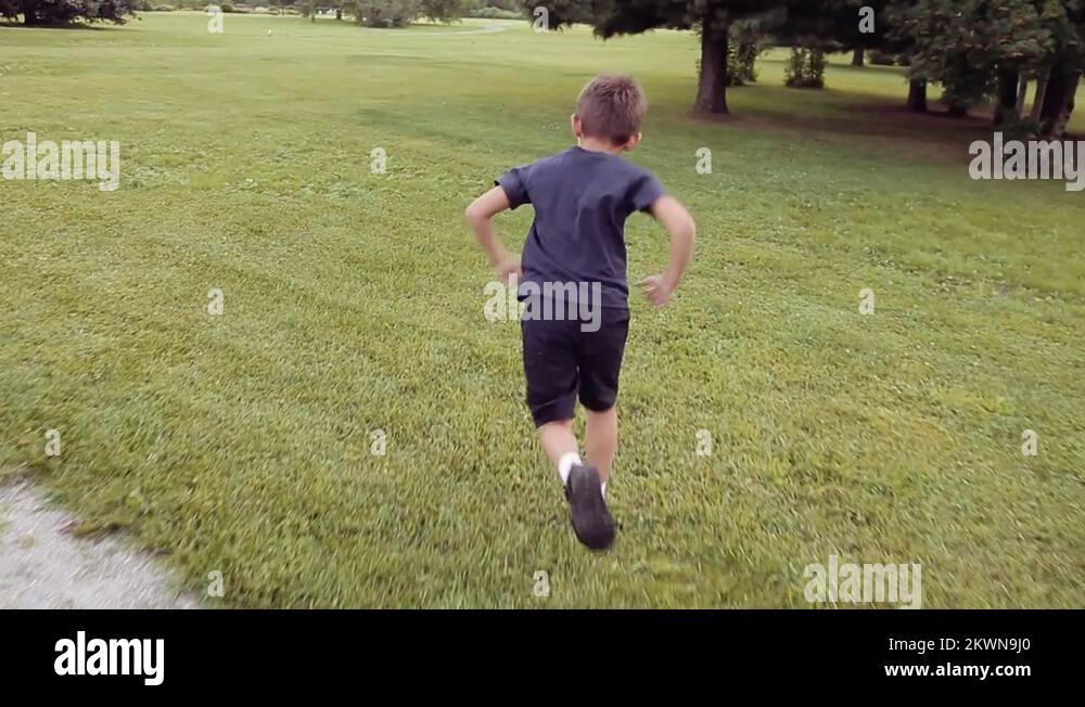 A little boy runs quickly across the grass falling and lying in a happy ...