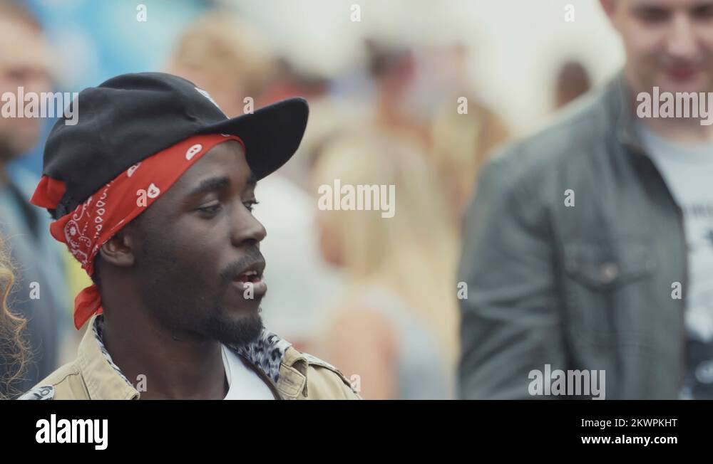 Bored young black man in gangster outfit posing with woman at crowded ...