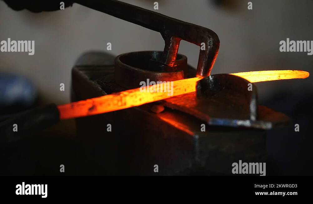 blacksmith working with hot glowing metal, bending steel in a smithery ...