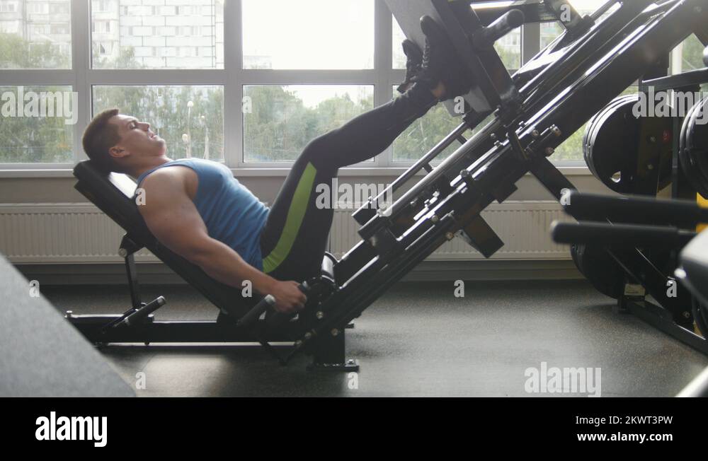 Fitness club - muscular man exercising on leg press machine - side view ...