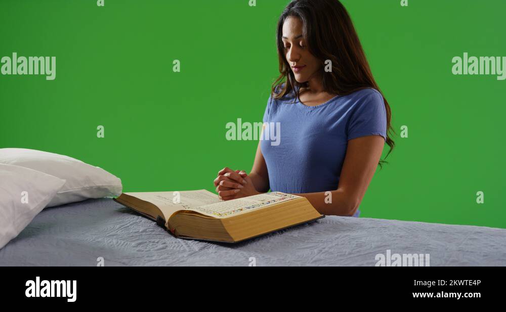 Latina woman sitting in her bedroom praying with open bible on green ...