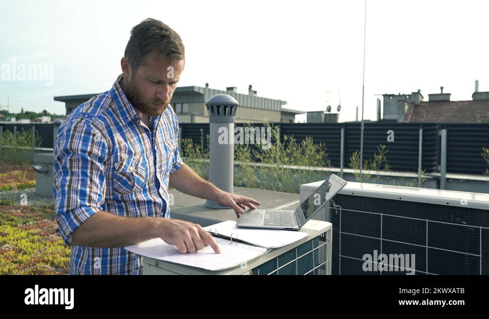 Man with laptop and blueprints checking air conditioning plan on roof ...