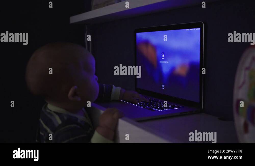 Baby boy pushes the button on laptop keyboard and types a password ...