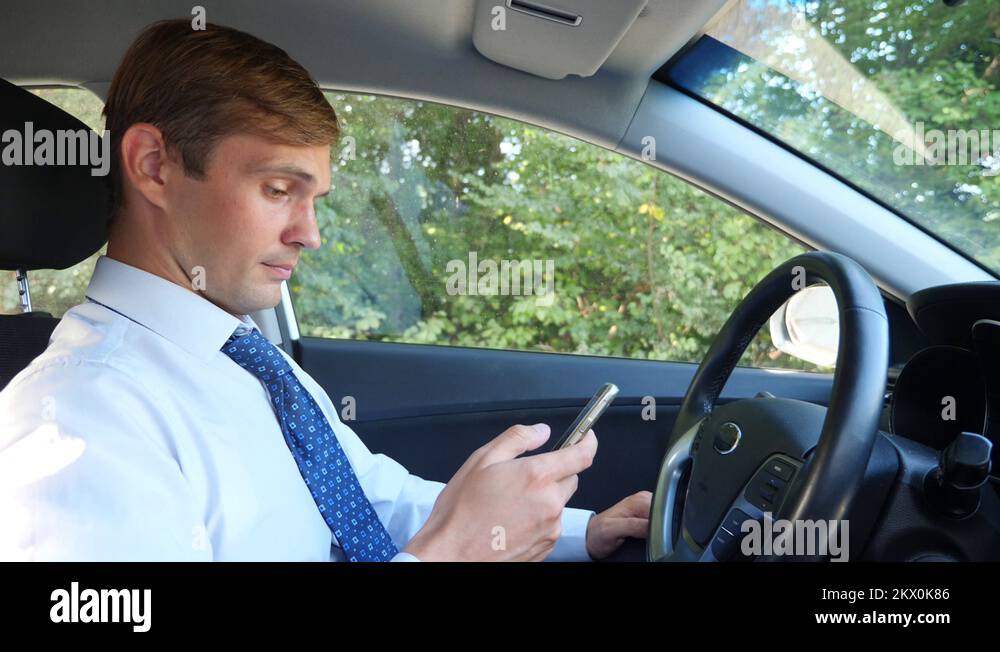 A male businessman in a shirt and tie is driving a car and browsing the ...