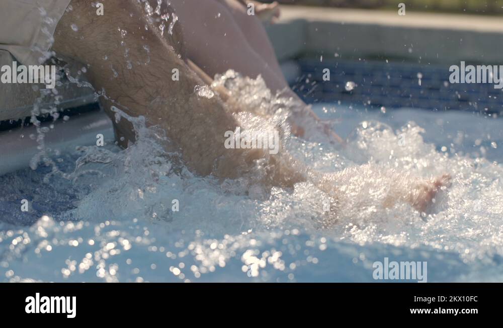 Detail of family's legs at side of swimming pool splashing feet in ...