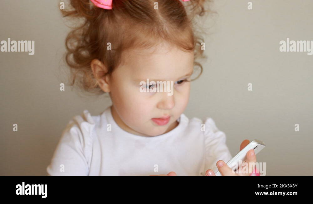 The child is holding a mobile phone, looking at the screen and touches ...