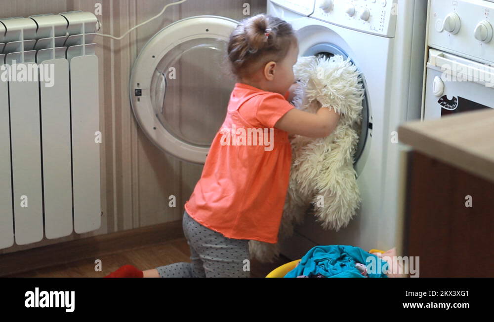 Funny cute little girl gets clean things from the washing machine. Baby ...
