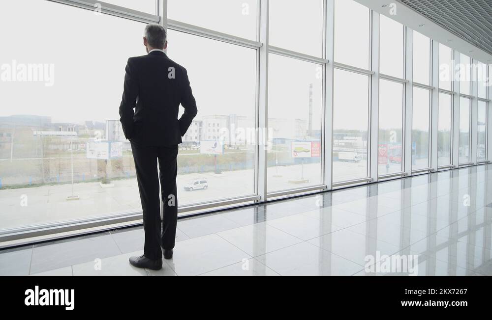 Man come and stand at full height, gaze out airport terminal window ...
